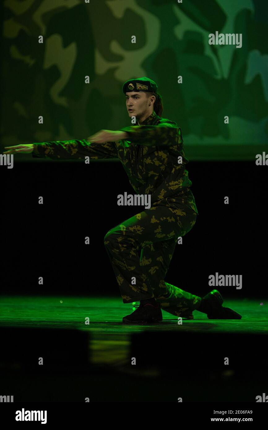 A young guy in military uniform is dancing on stage in a stage light ...