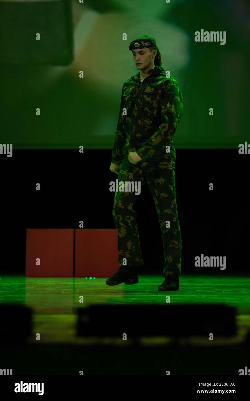 A young guy in military uniform is dancing on stage in a stage light ...