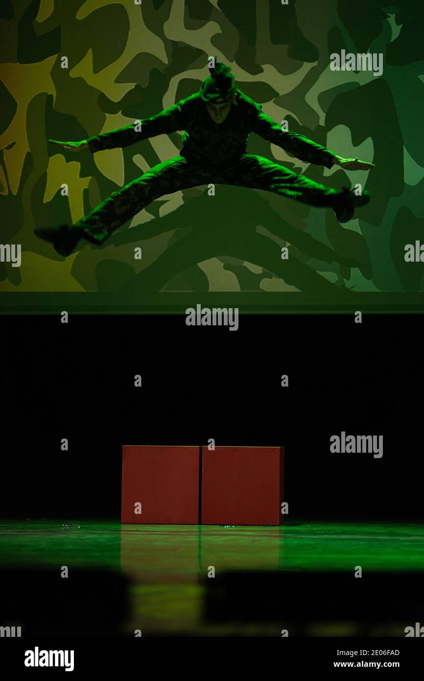 A young guy in military uniform is dancing on stage in a stage light ...