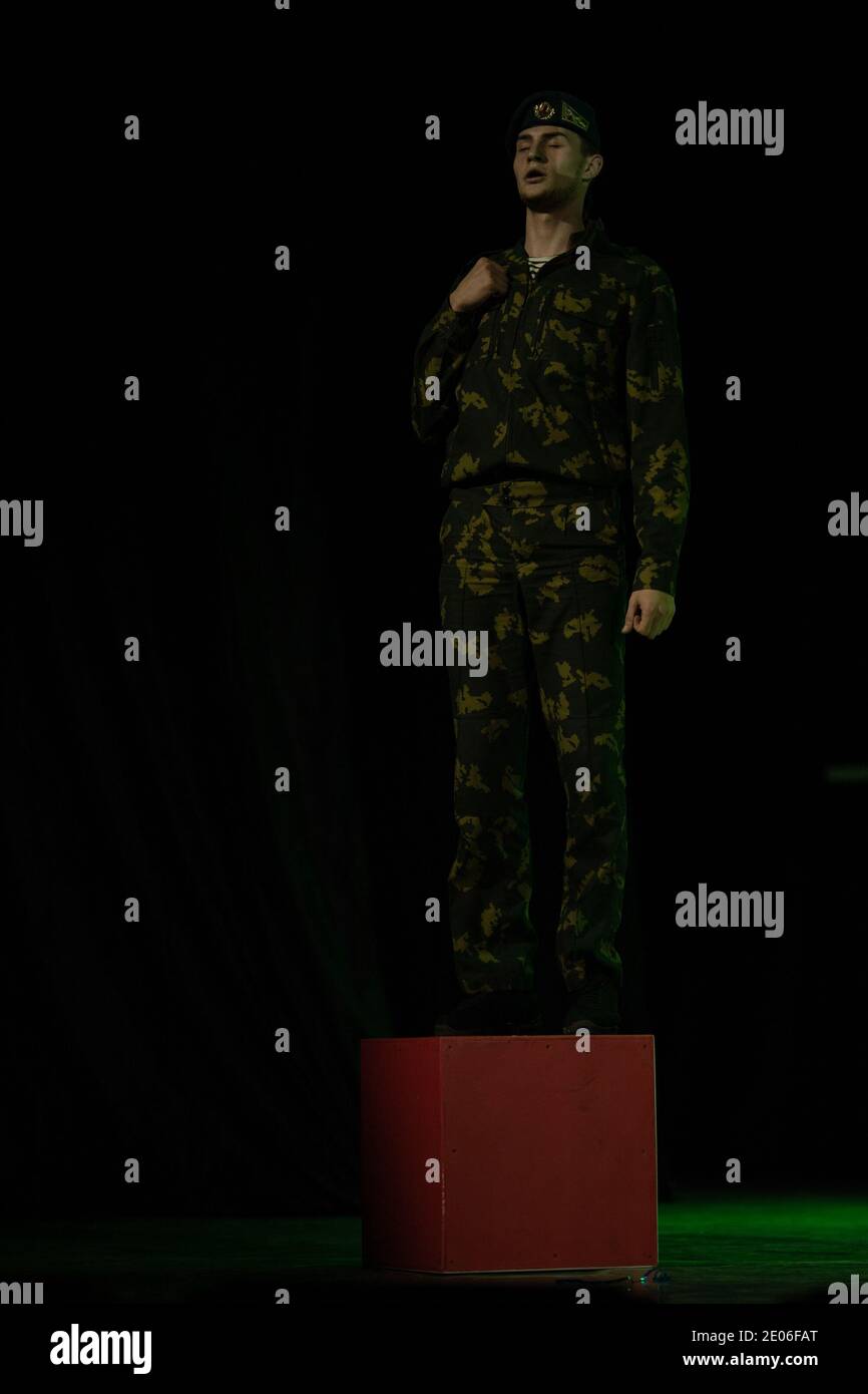 A young guy in military uniform is dancing on stage in a stage light ...