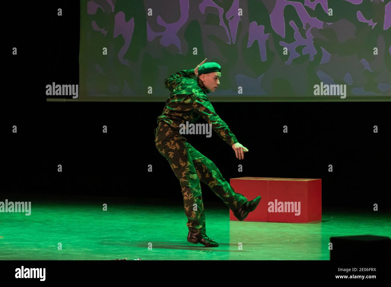 A young guy in military uniform is dancing on stage in a stage light ...