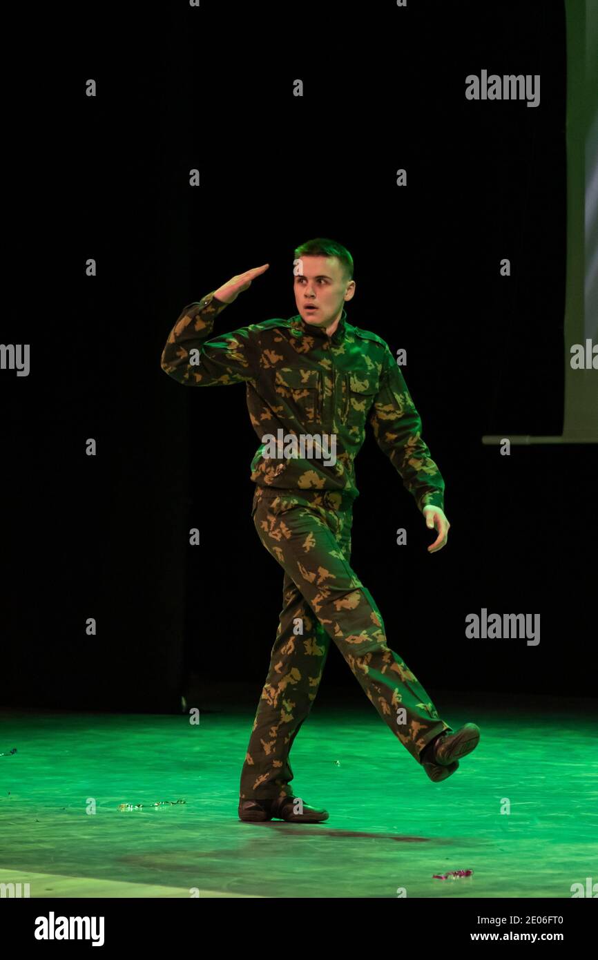 A young guy in military uniform is dancing on stage in a stage light ...