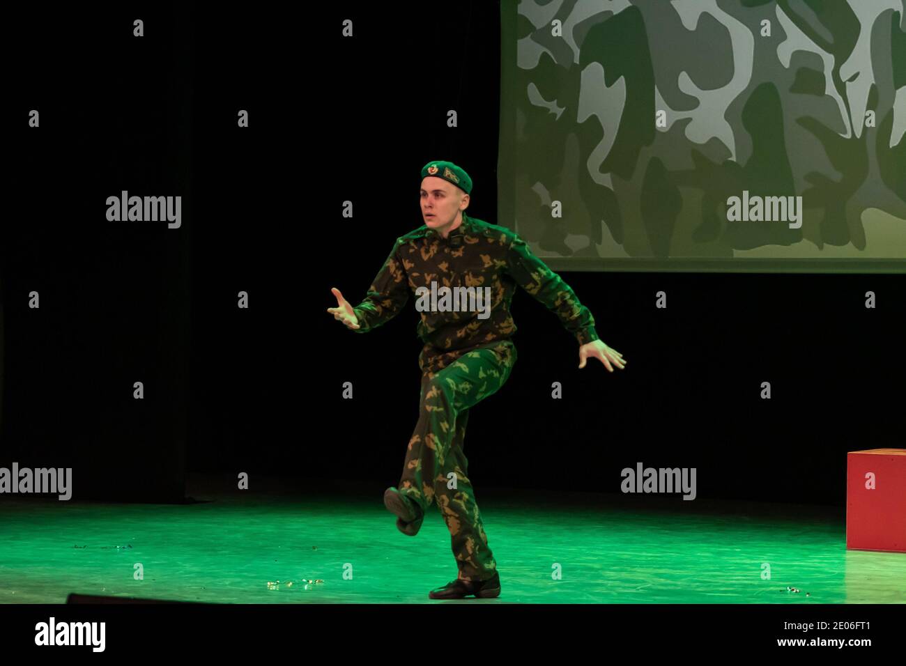 A young guy in military uniform is dancing on stage in a stage light ...