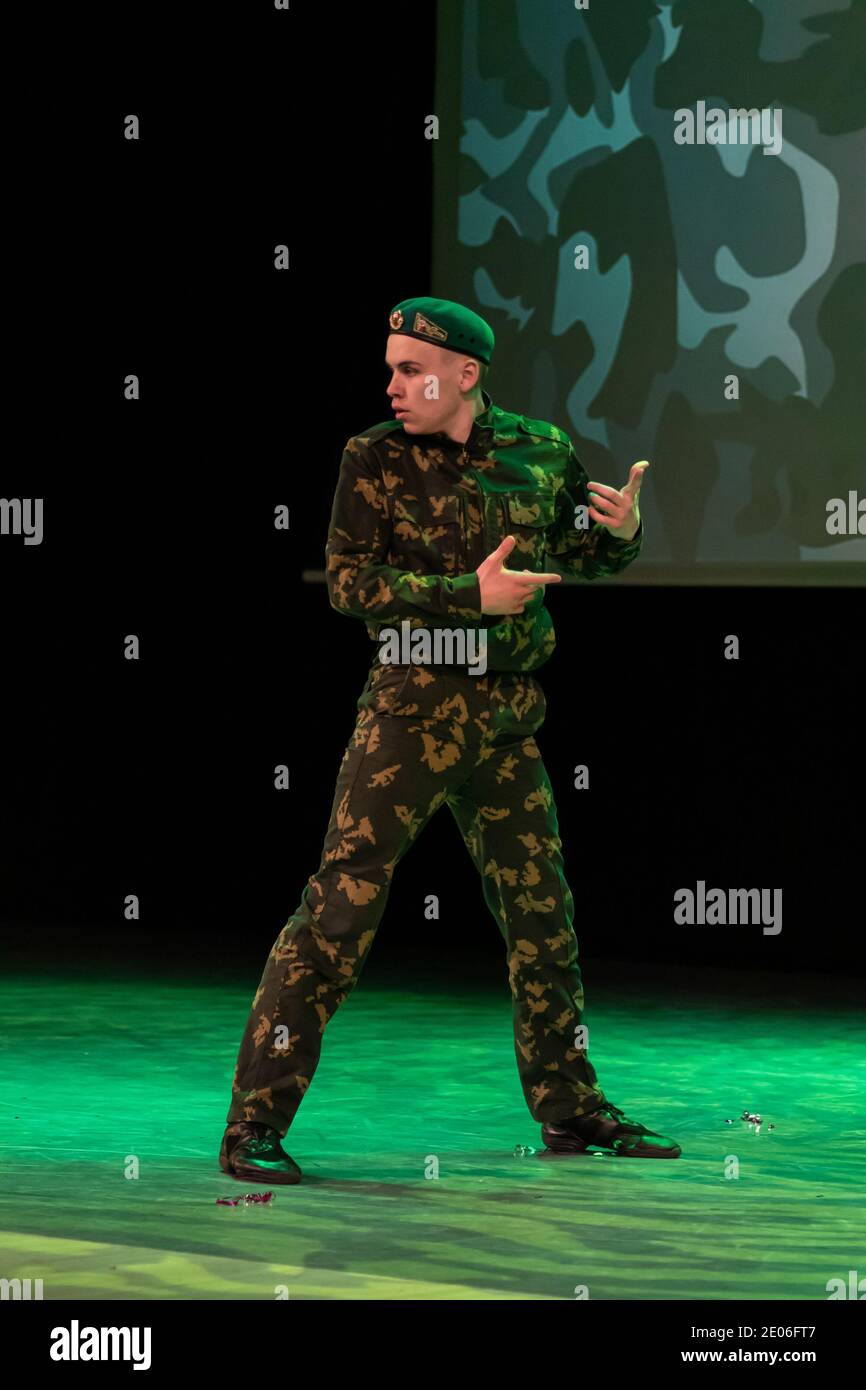 A young guy in military uniform is dancing on stage in a stage light ...