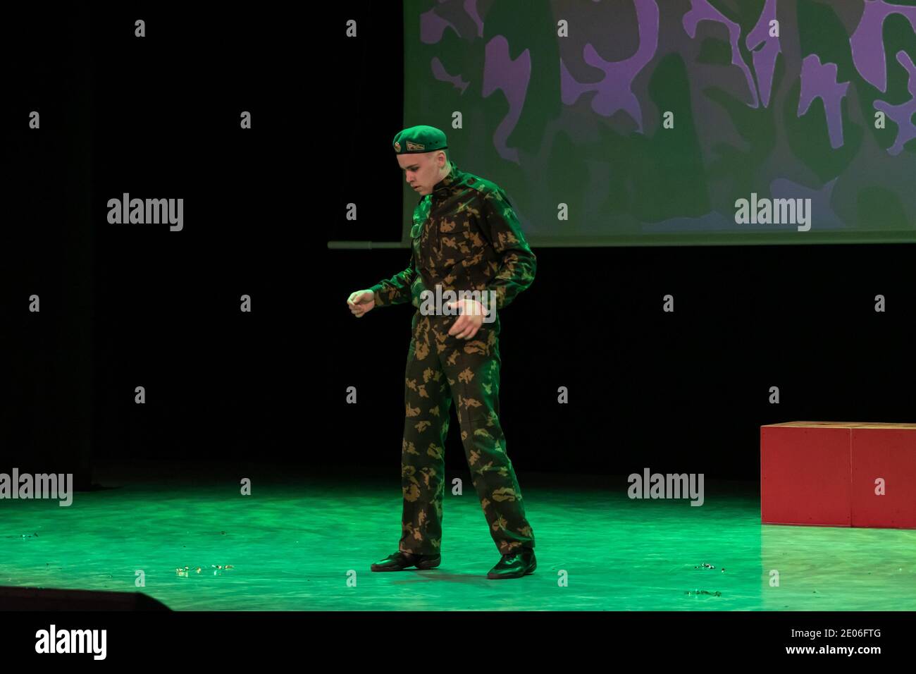 A young guy in military uniform is dancing on stage in a stage light ...