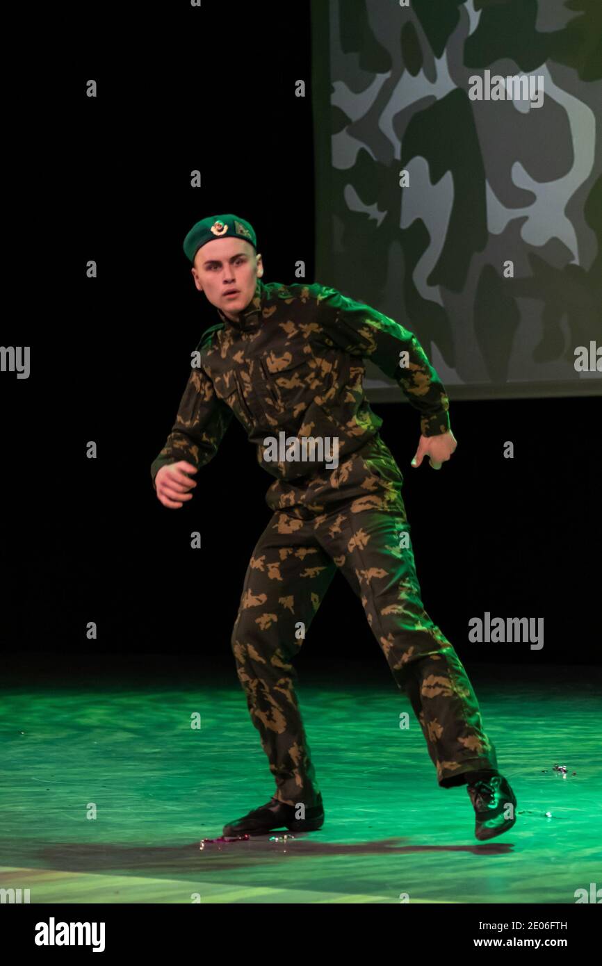 A young guy in military uniform is dancing on stage in a stage light ...