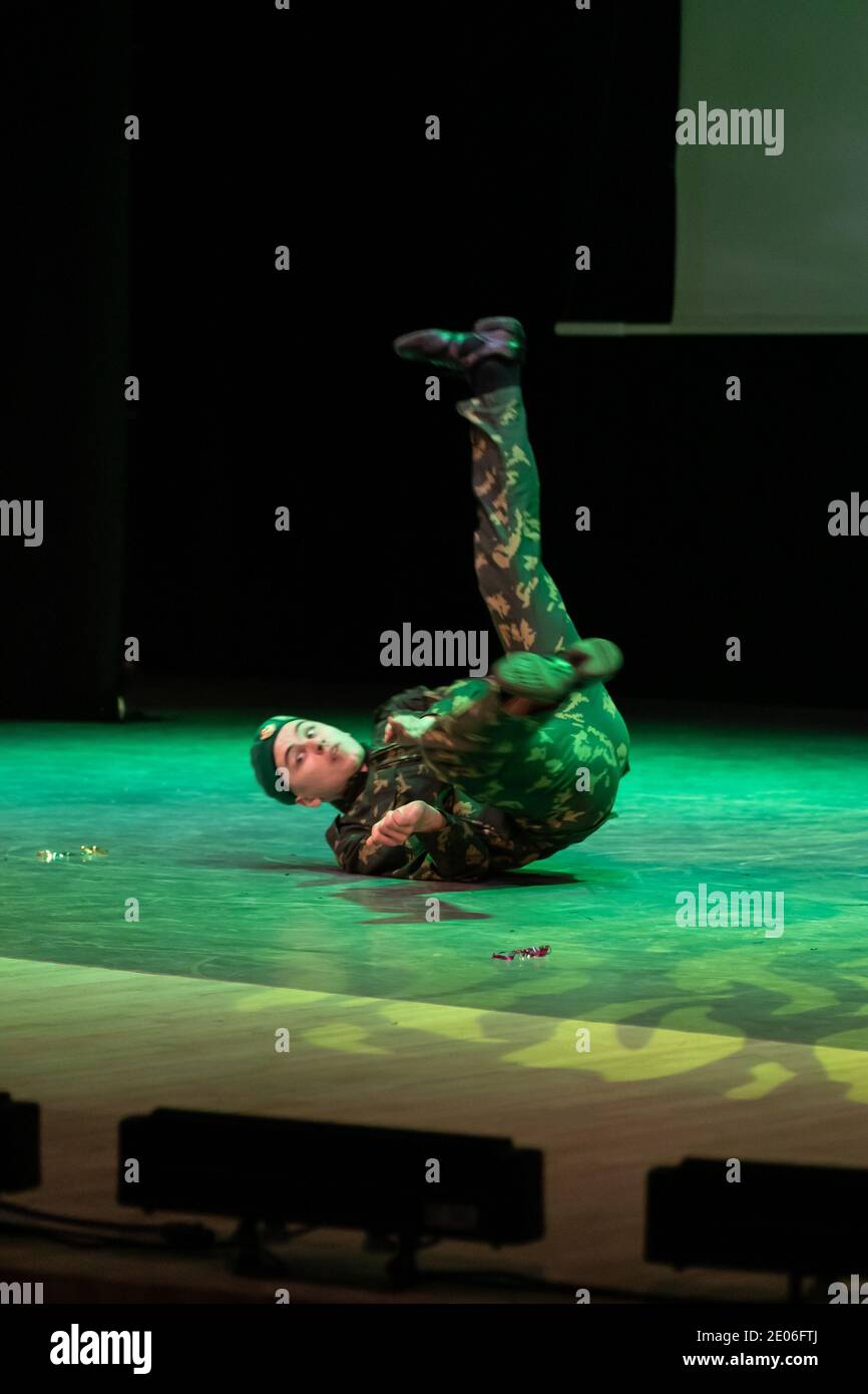 A young guy in military uniform is dancing on stage in a stage light ...