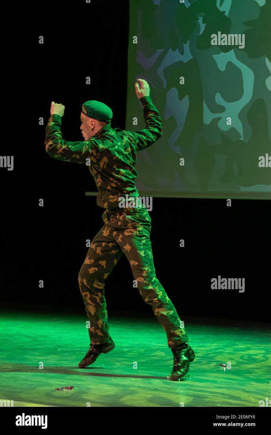 A young guy in military uniform is dancing on stage in a stage light ...