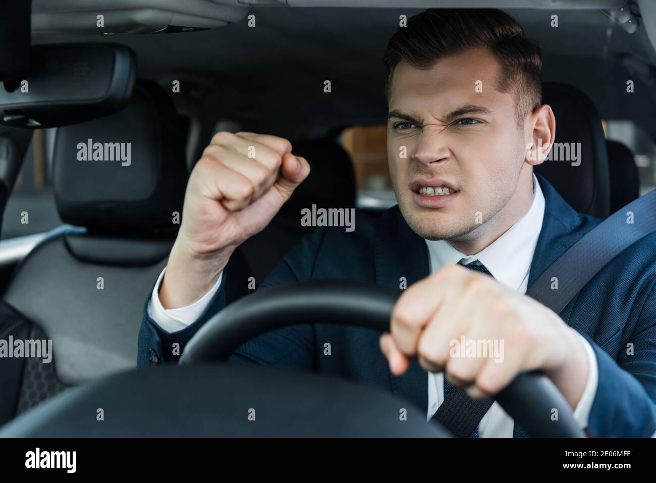 Angry businessman showing fist while driving auto on blurred foreground ...