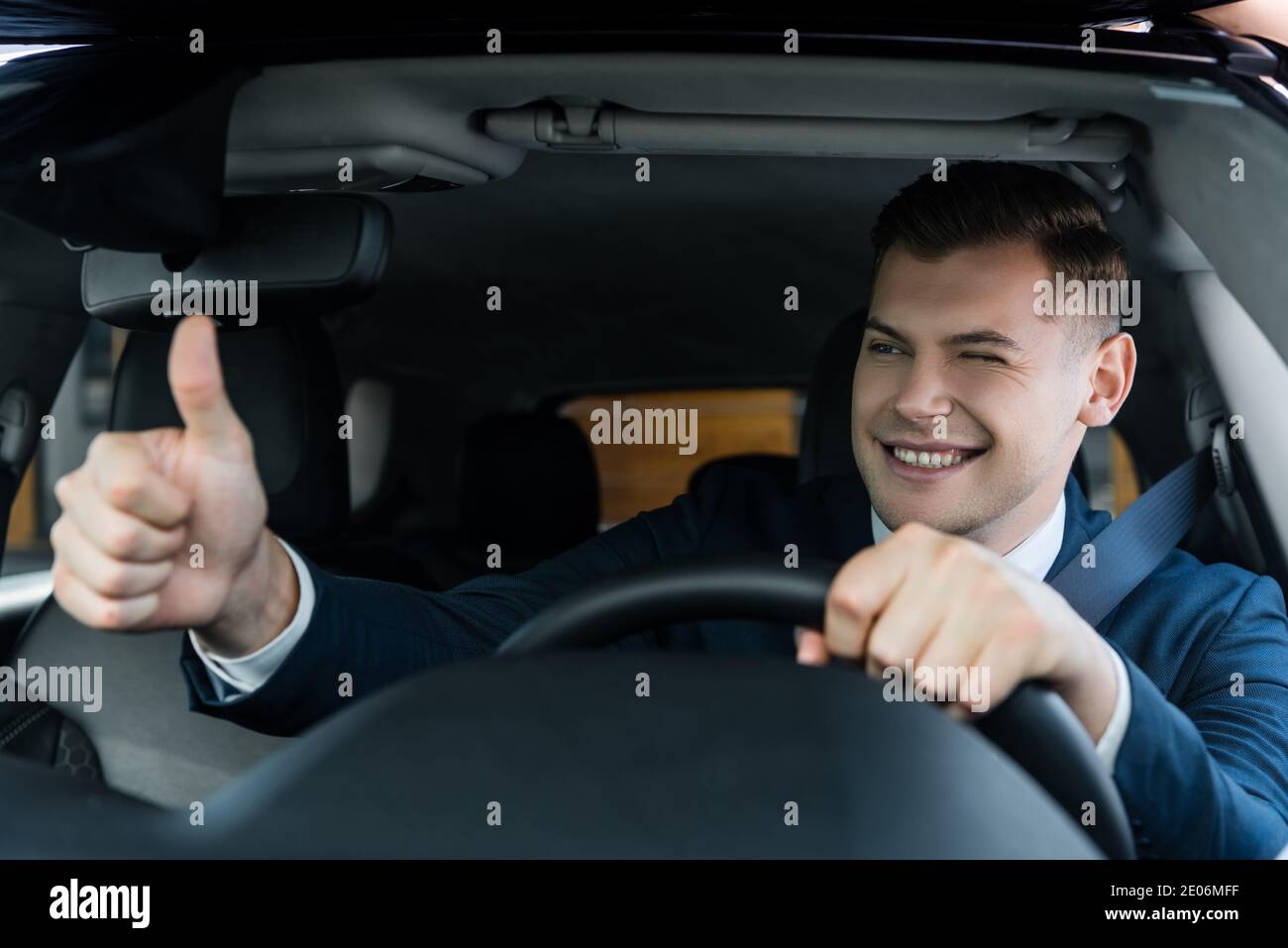Smiling businessman winking and showing like gesture while driving car ...