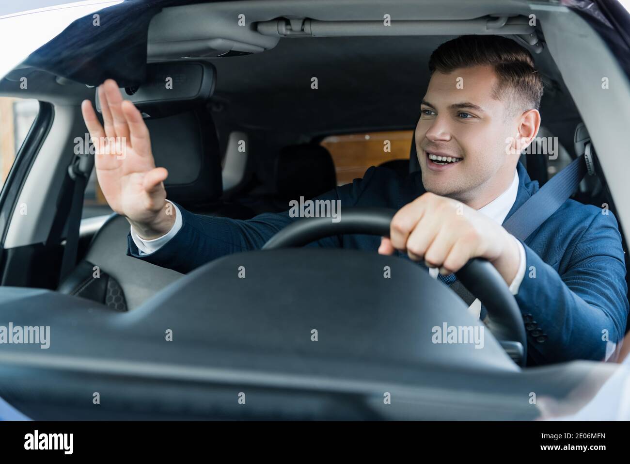 Cheerful businessman waving hand while driving car on blurred ...
