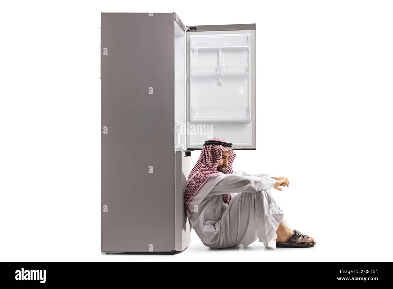 Sad saudi arab man sitting on the floor and leaning on an empty fridge ...