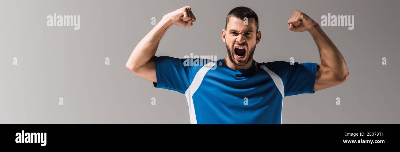 Excited sportsman with open mouth showing yeah gesture isolated on grey ...