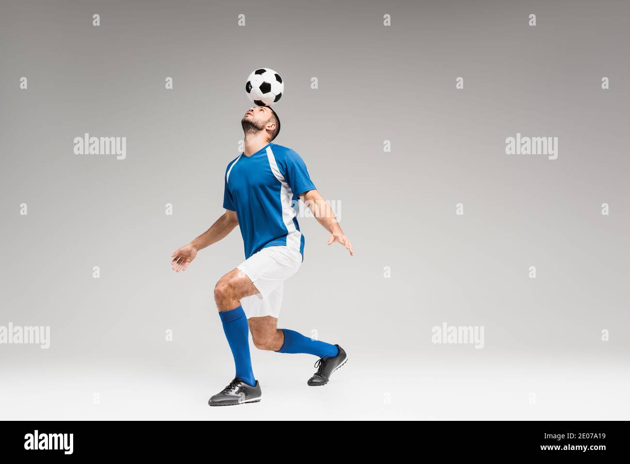 Sportsman holding football on head while balancing on grey background ...