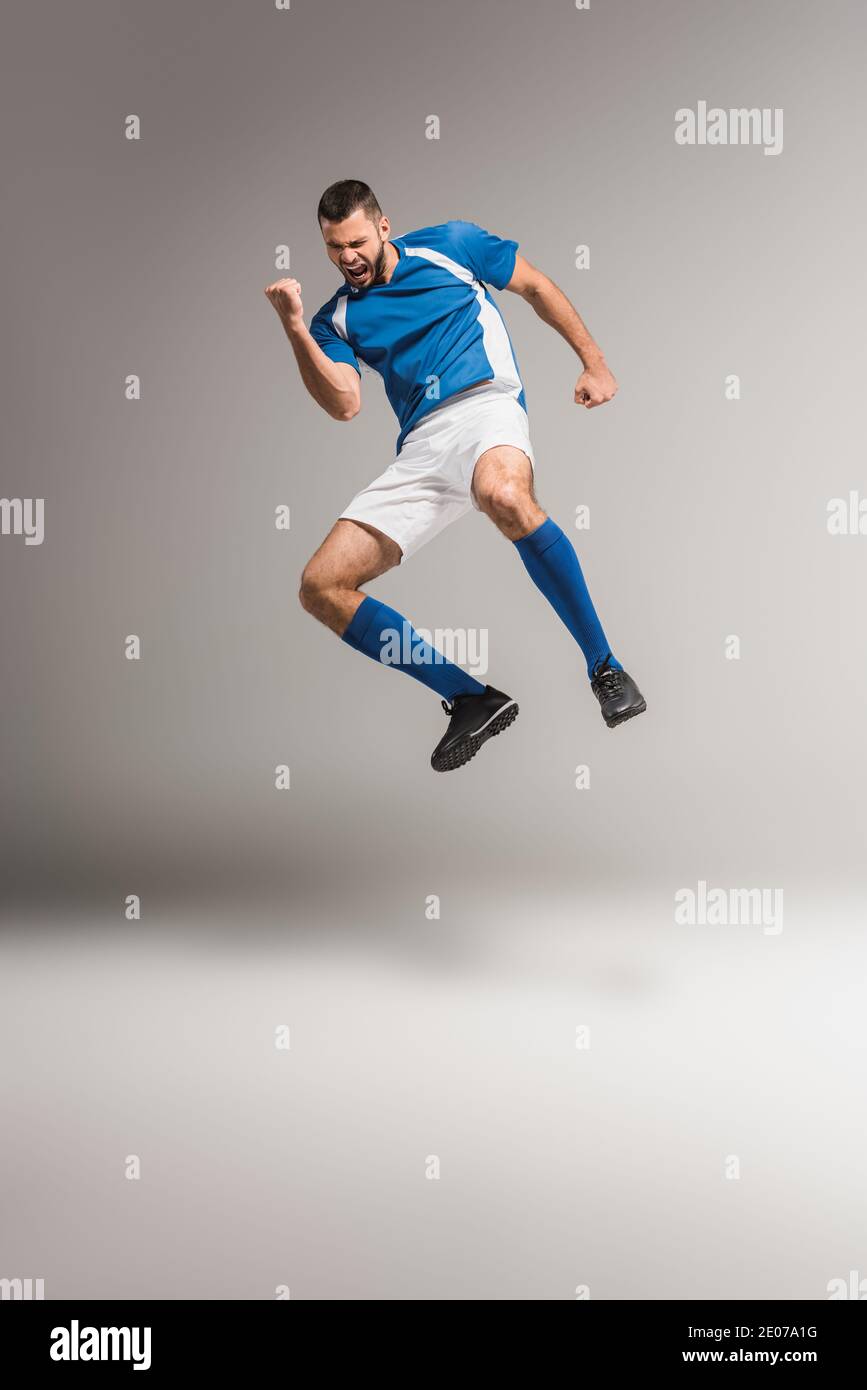 Athletic man showing yeah gesture while jumping on grey background ...