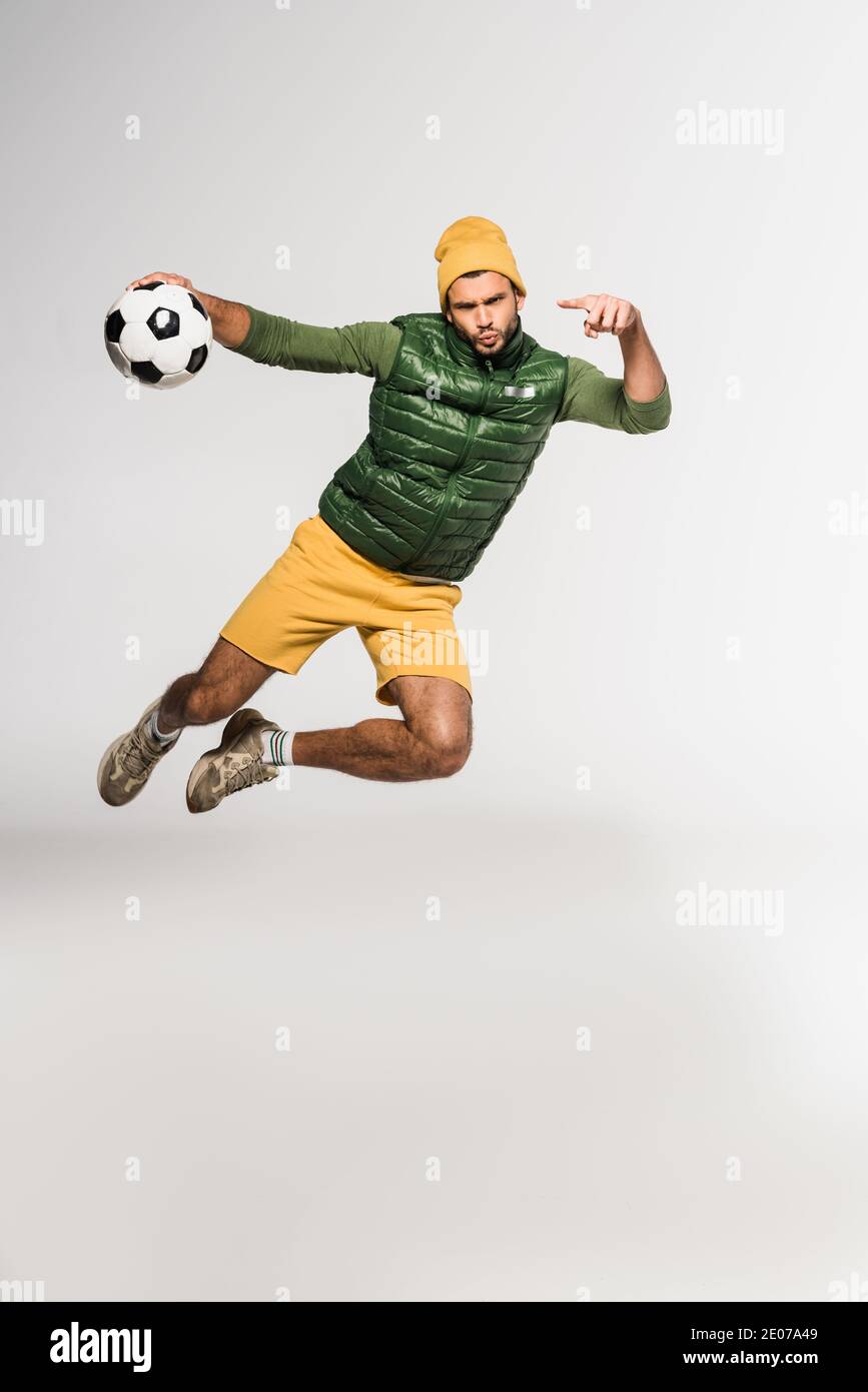 Sportsman pointing with finger at football mid air on grey background ...