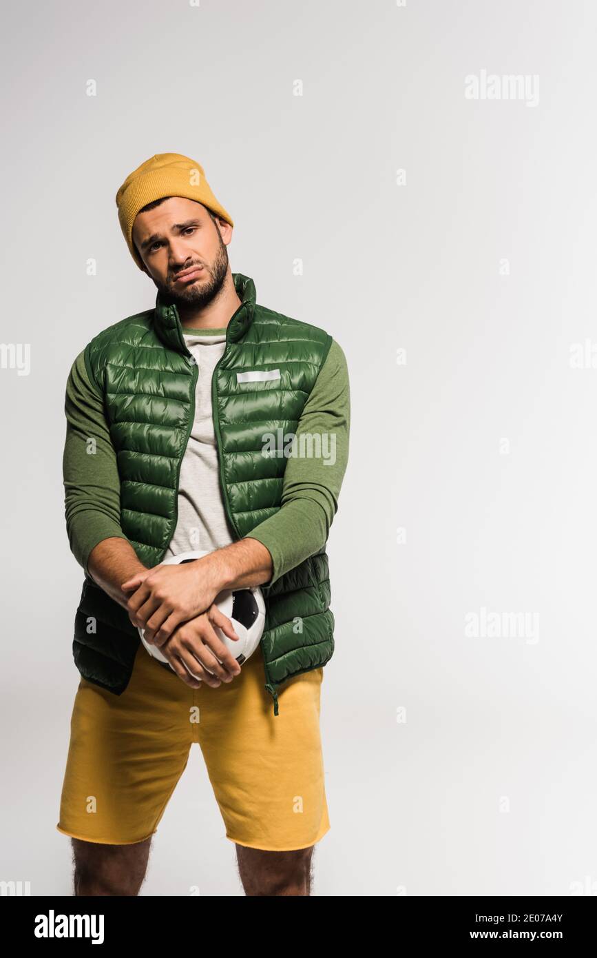 Sad sportsman holding football and looking at camera isolated on grey ...
