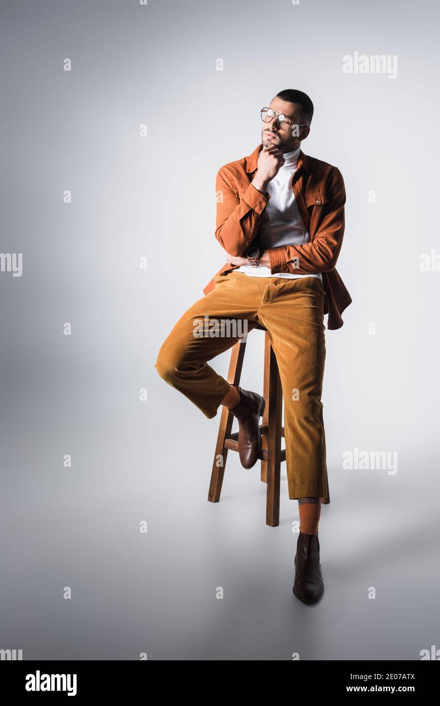 Pensive stylish man sitting on chair on grey background Stock Photo - Alamy