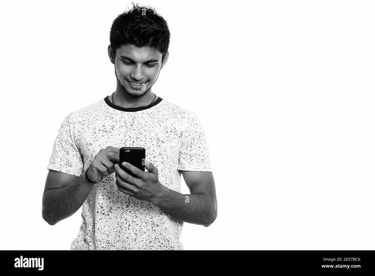 Studio shot of young happy Indian man smiling while using mobile phone ...