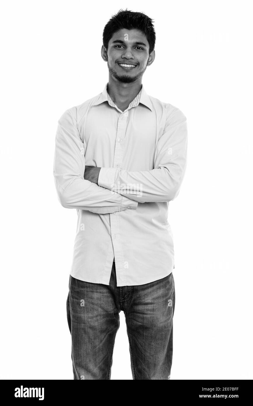 Studio shot of young happy Indian man smiling and standing with arms ...