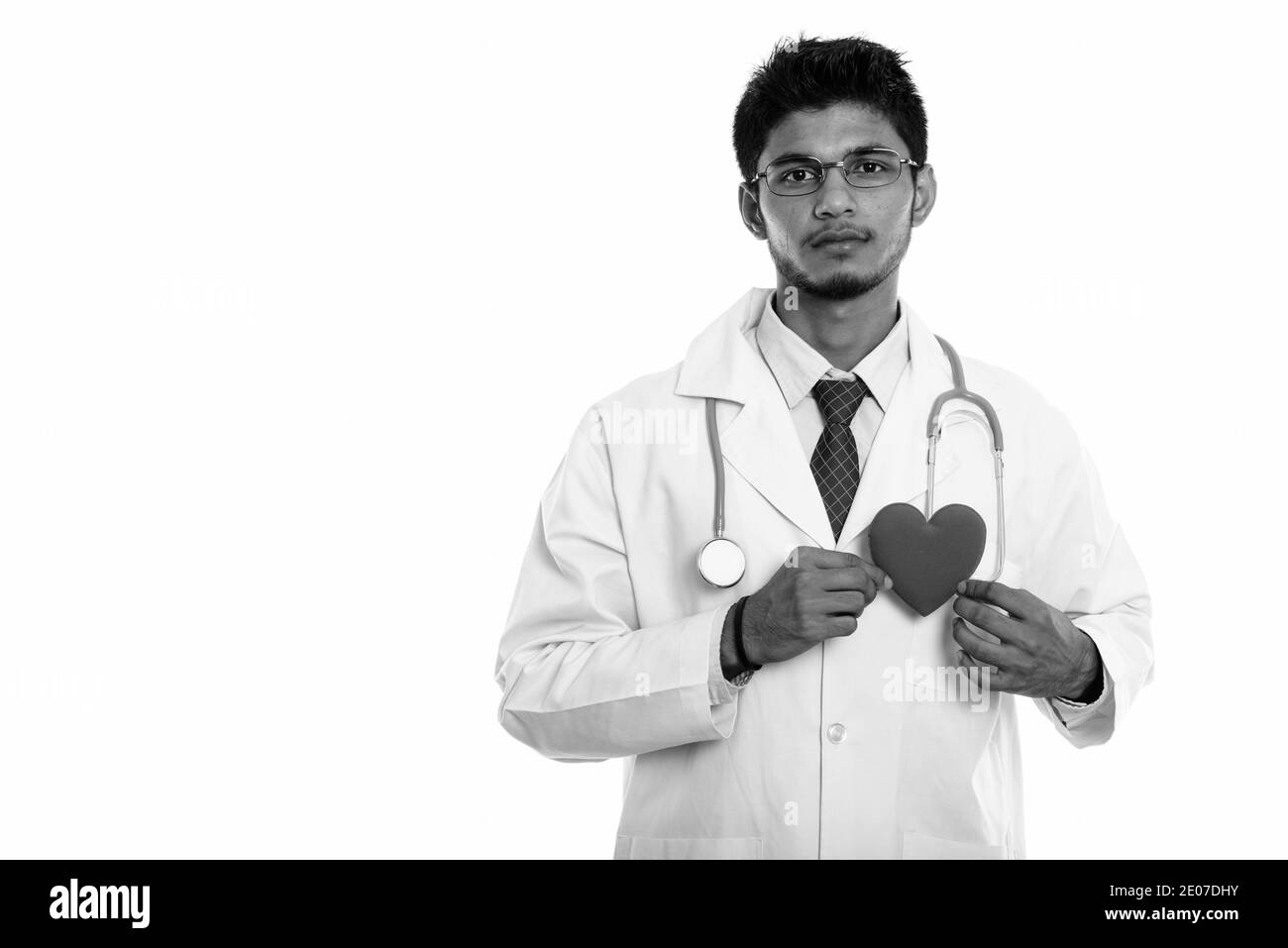 Studio shot of young handsome Indian man doctor holding red heart ...