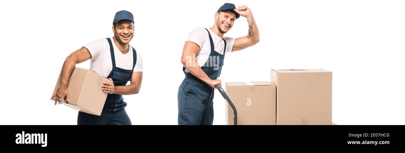 excited multicultural movers in uniform and caps near hand truck with ...