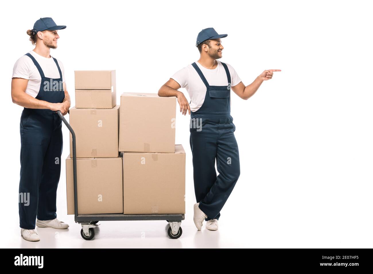 full length of happy indian mover in uniform and cap pointing with ...