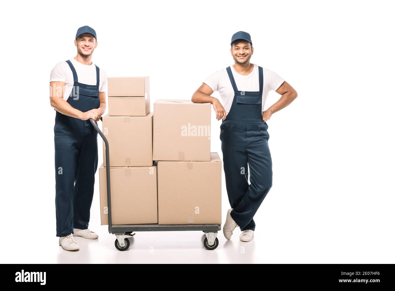 full length of joyful multicultural movers in uniform and caps standing ...