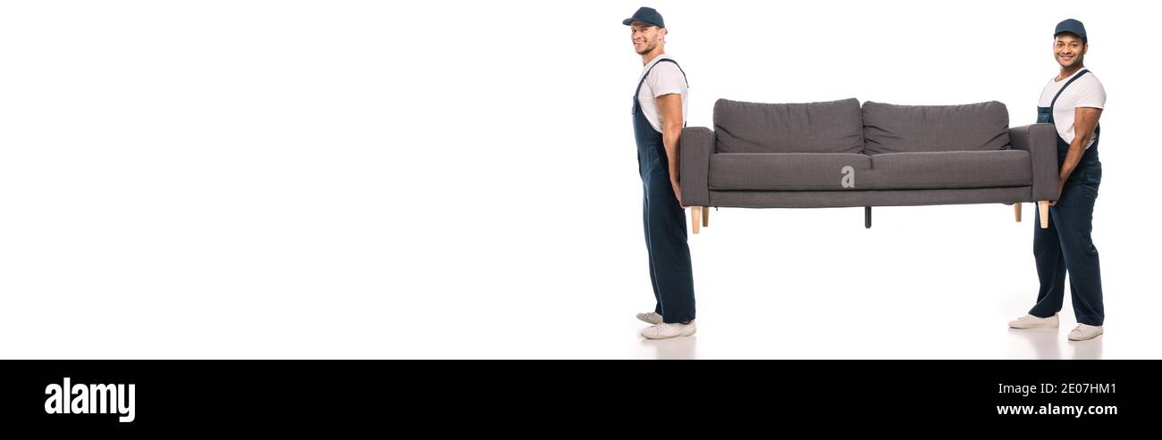 full length of cheerful multicultural movers carrying couch on white ...