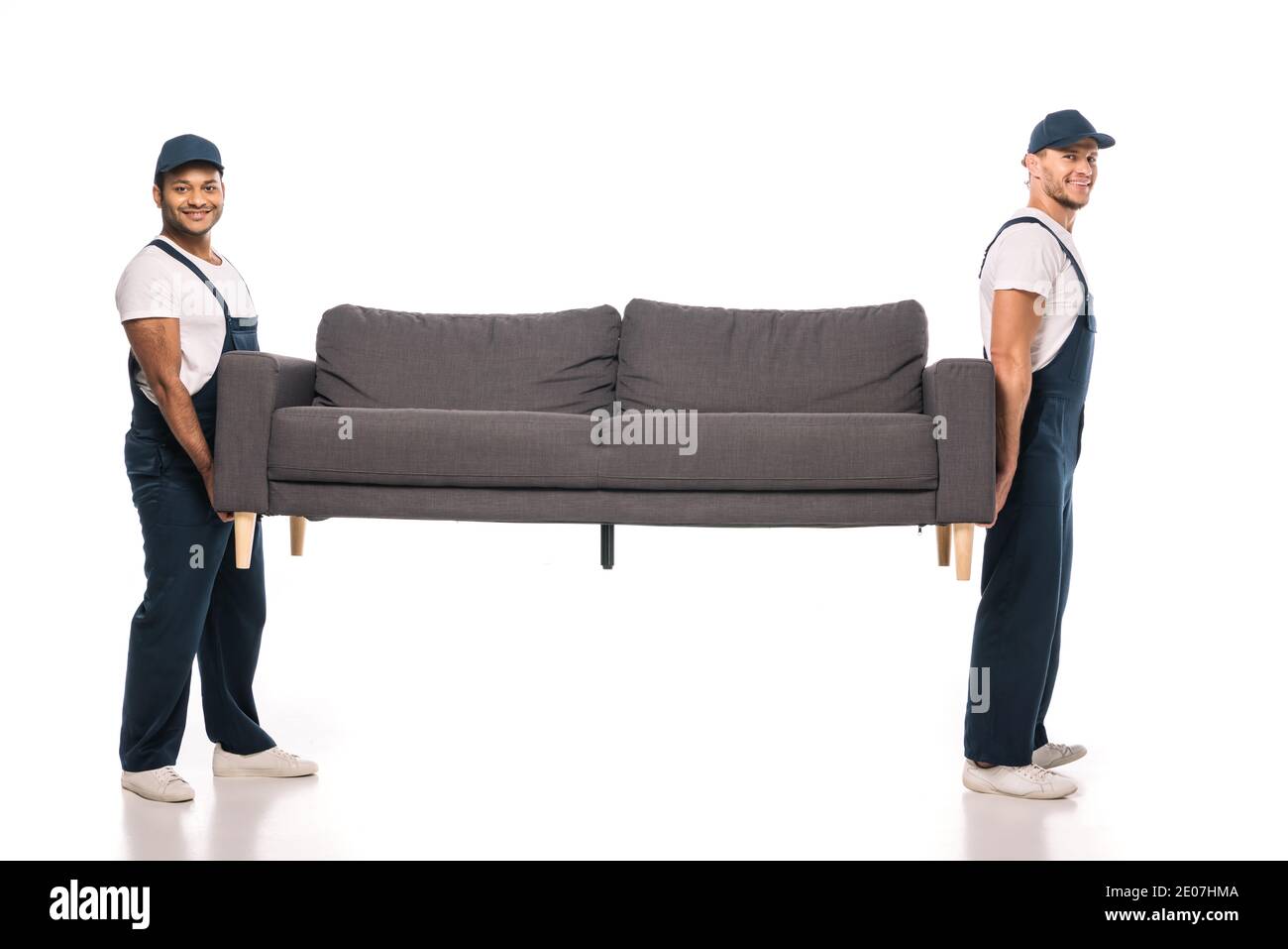 full length of cheerful multicultural movers carrying couch on white ...