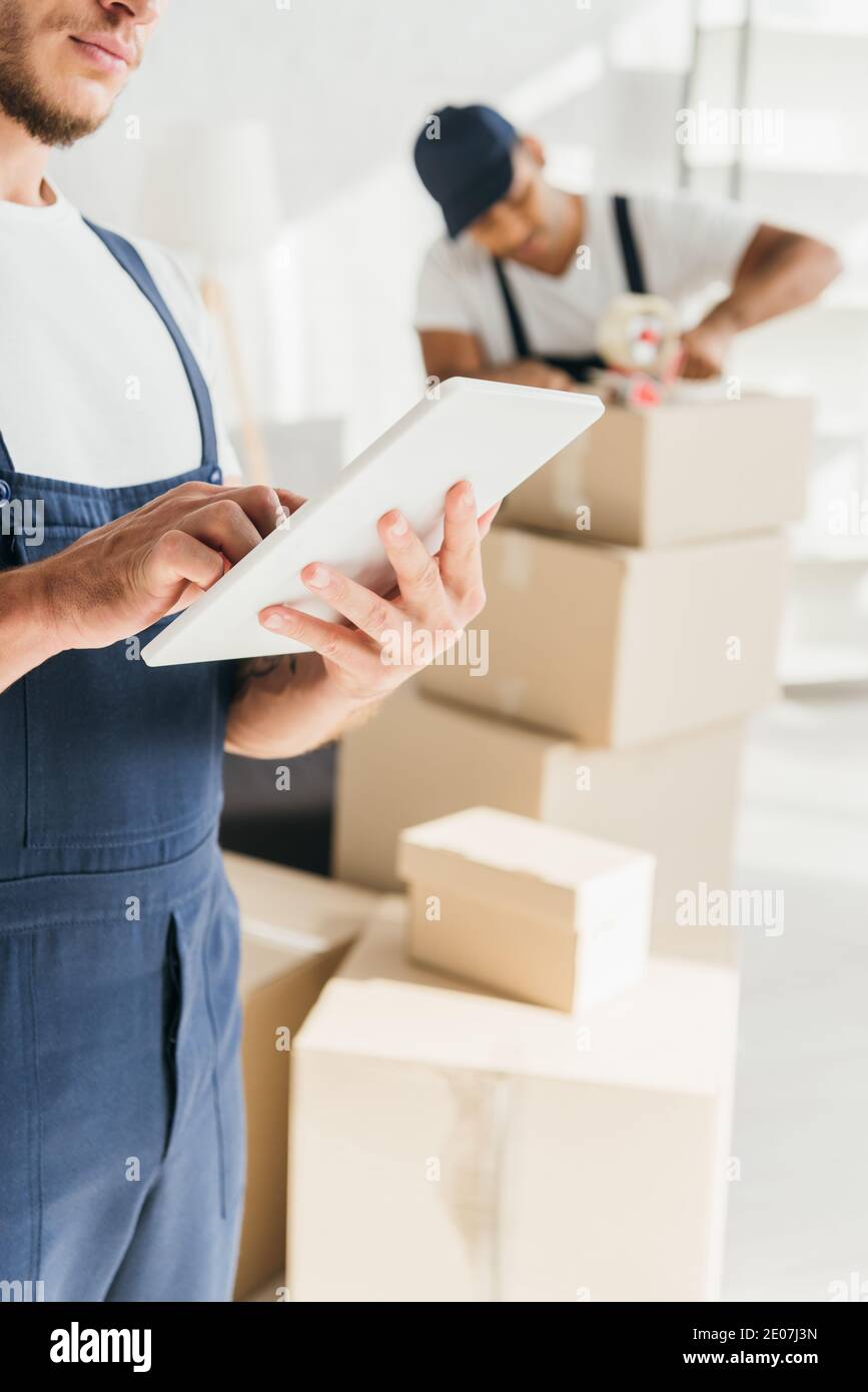 cropped view of worker in uniform holding digital tablet near indian ...