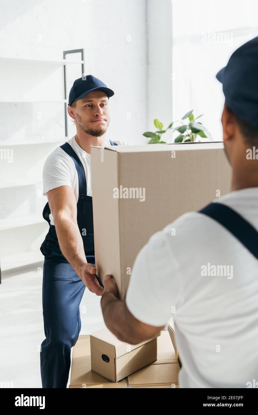 young worker in uniform receiving carton box from indian coworker on ...