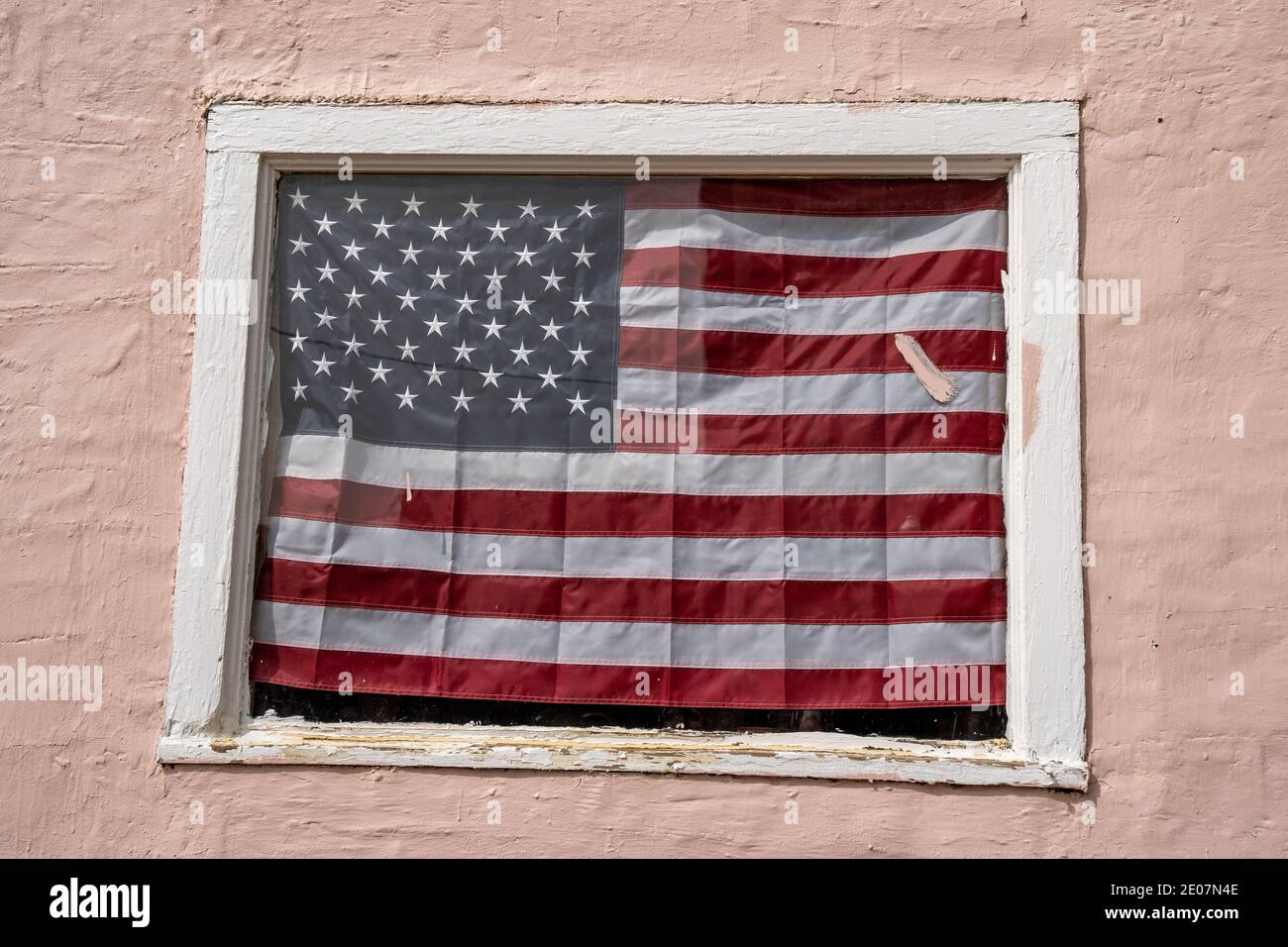 An American flag hanging in a window on a peach painted building Stock ...