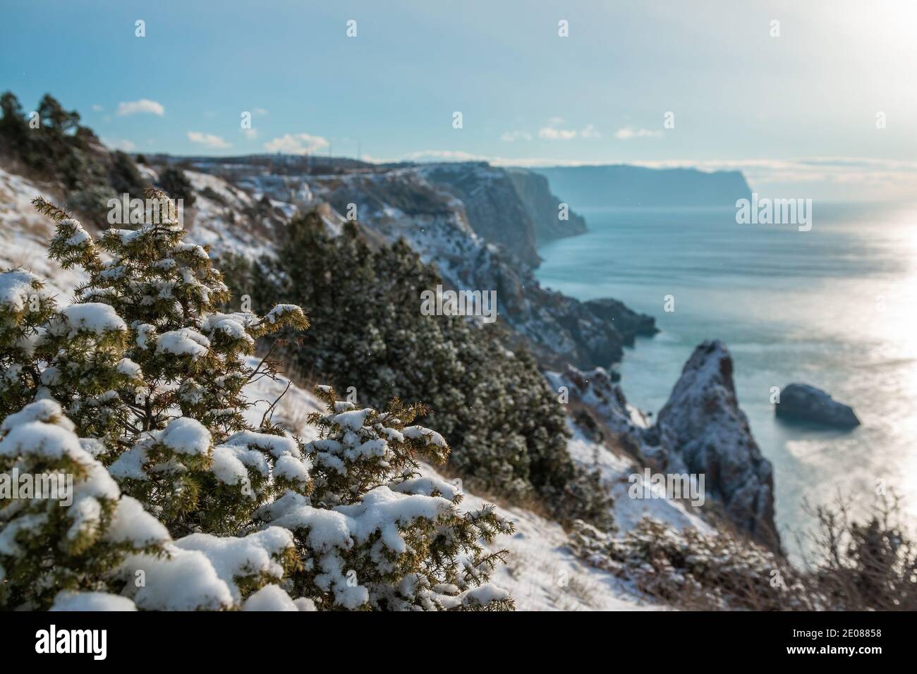 Snow covered rocky cliffs over sea. Winter sunset over the sea bay ...
