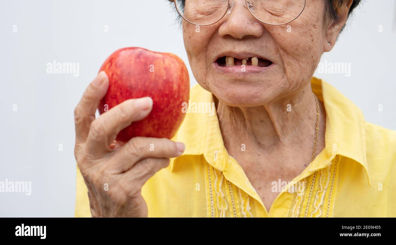 An old woman wears glasses and without teeth trying to eat red apples ...