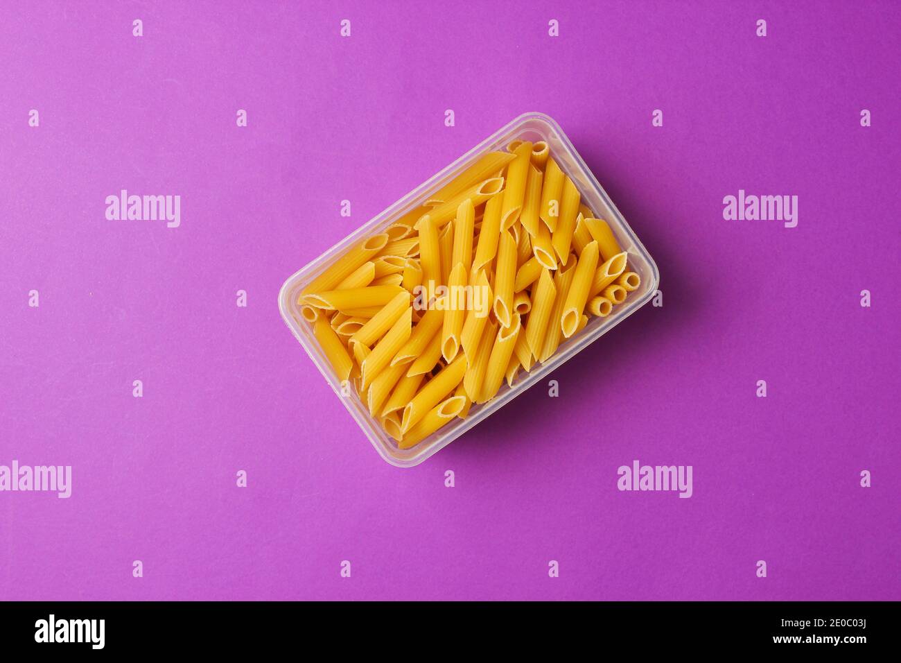 Penne rigata pasta in container on purple background. Top view Stock ...