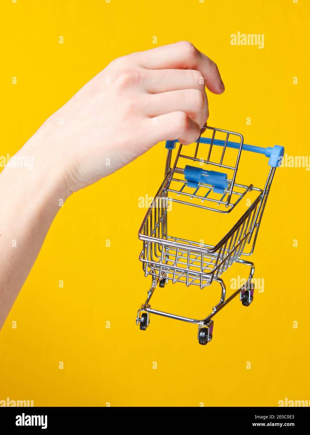 Female hand holding a mini shopping trolley on yellow background ...