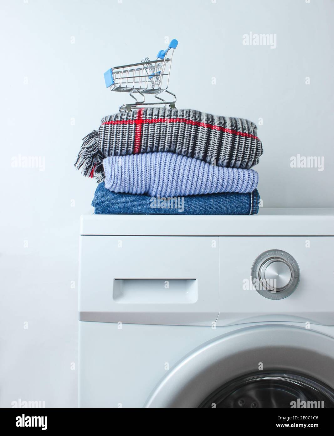 Stack of clothes, mini shopping cart on washing machine against a white ...