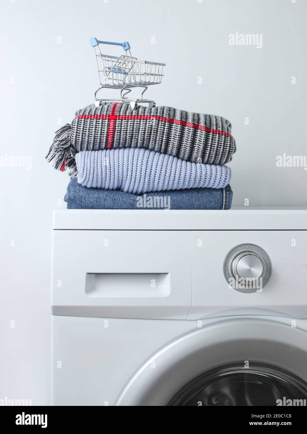 Stack of clothes, mini shopping cart on washing machine against a white ...