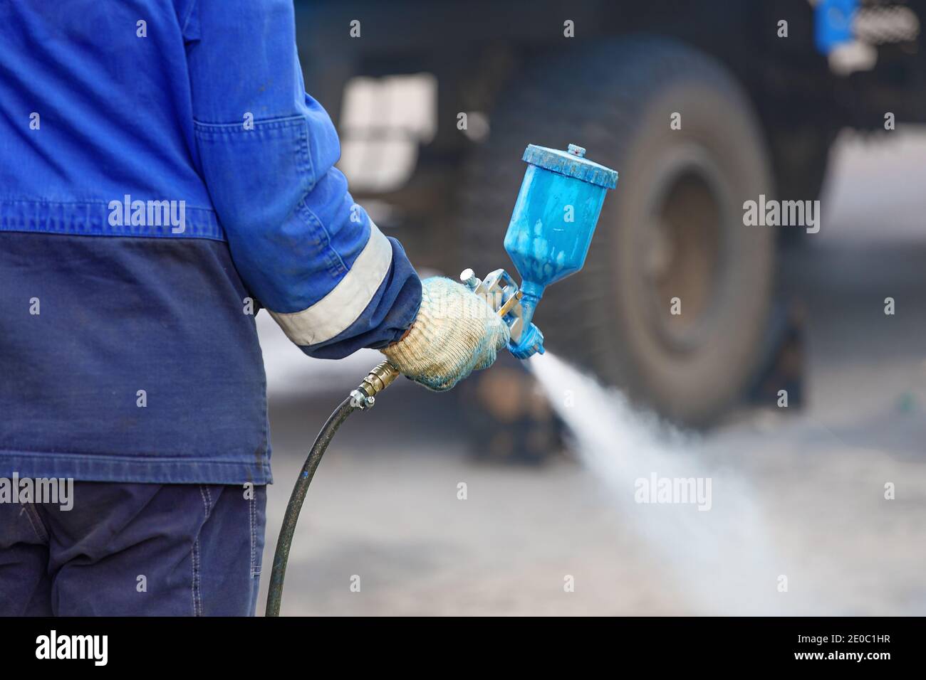 Spray gun in hand. A worker in overalls and a glove holds a spray ...