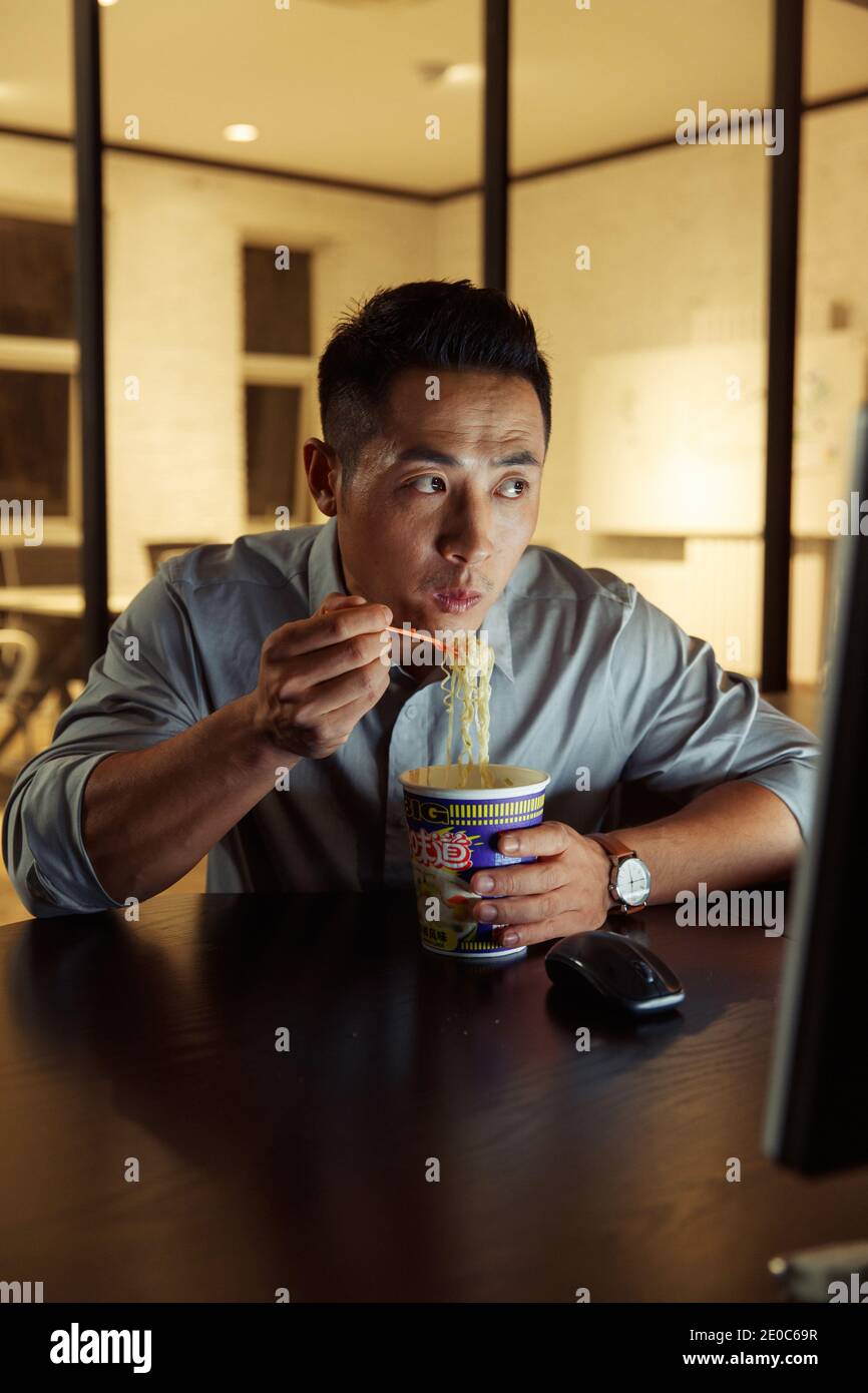 Young men in the office to work overtime to eat instant noodles Stock ...