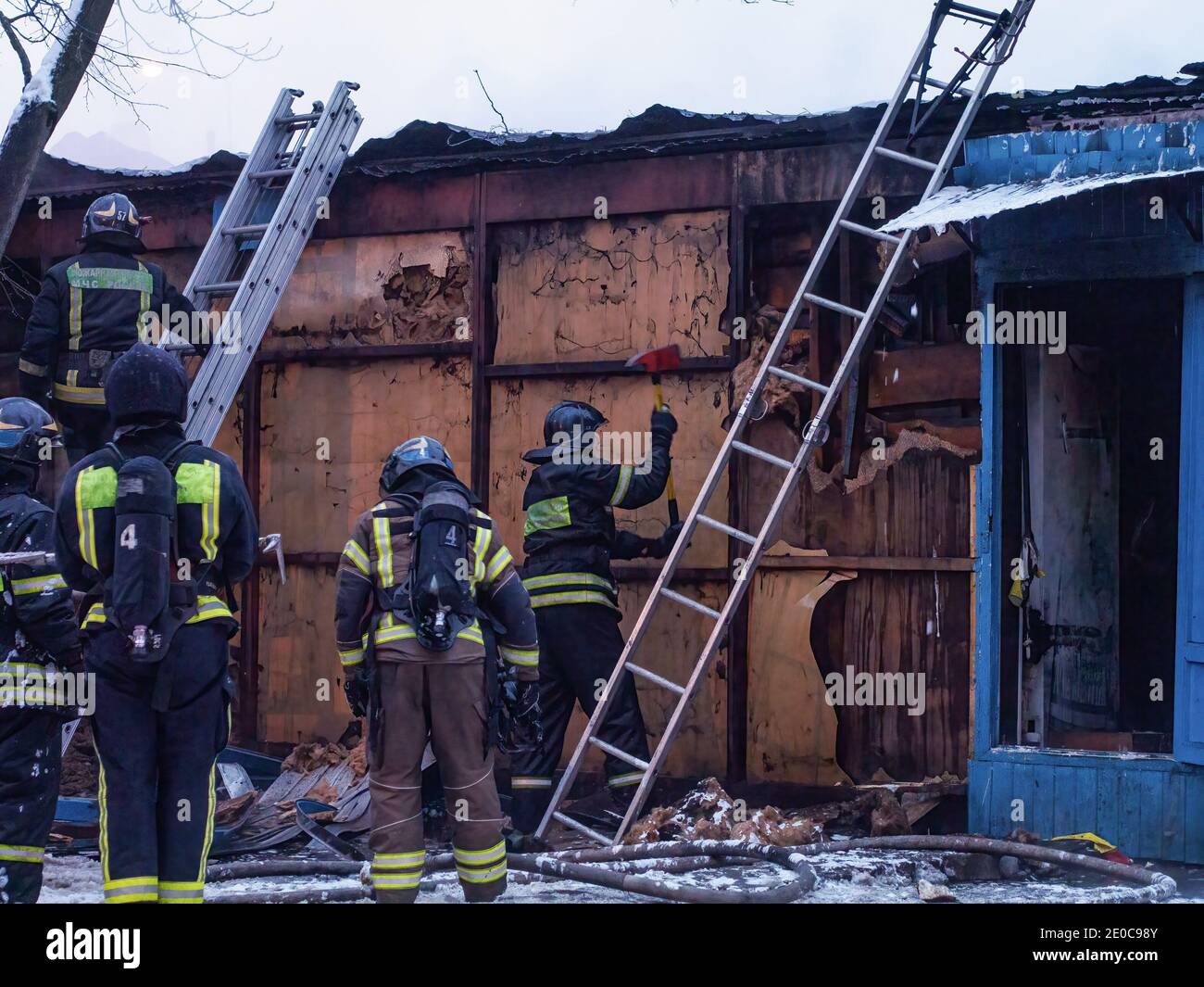 Firefighters break open the wall cladding of a burnt-out cafe. A fire ...