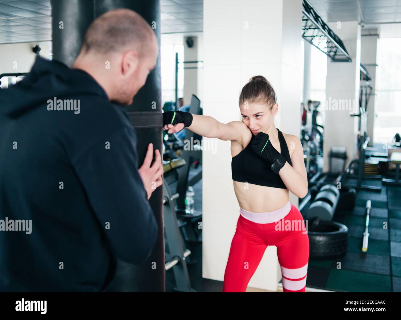 Male instructor trains young woman to do hand punches at punching bag ...