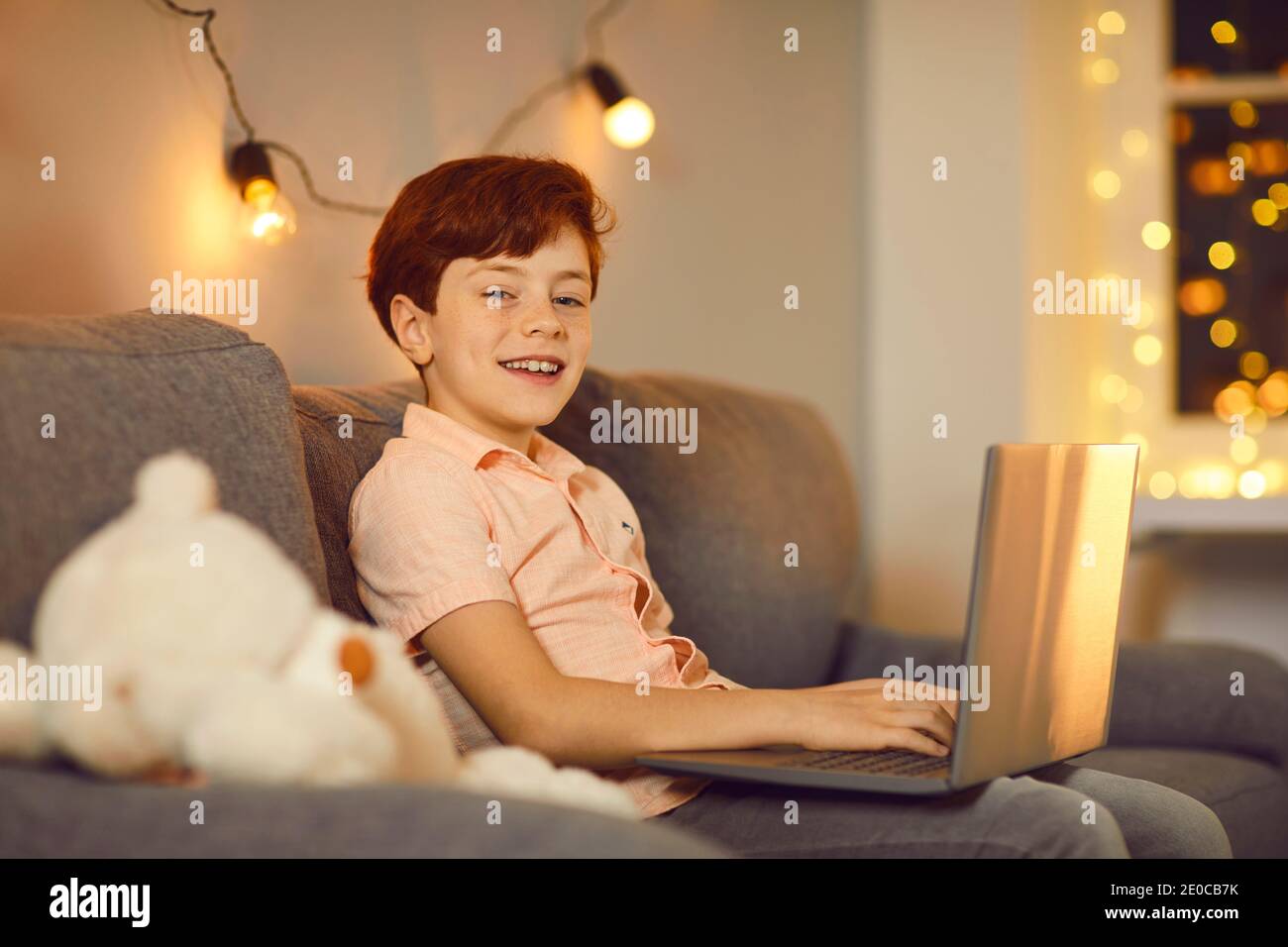 Cute smiling boy sitting with laptop at home on sofa and corresponding ...