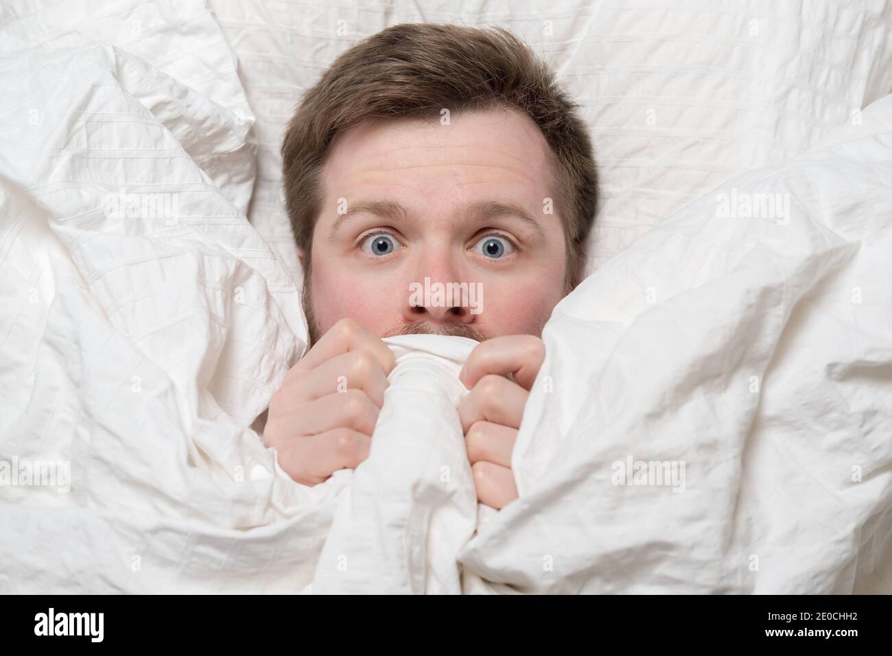 Nightmare. Caucasian man is scared, he hides under the covers and looks ...