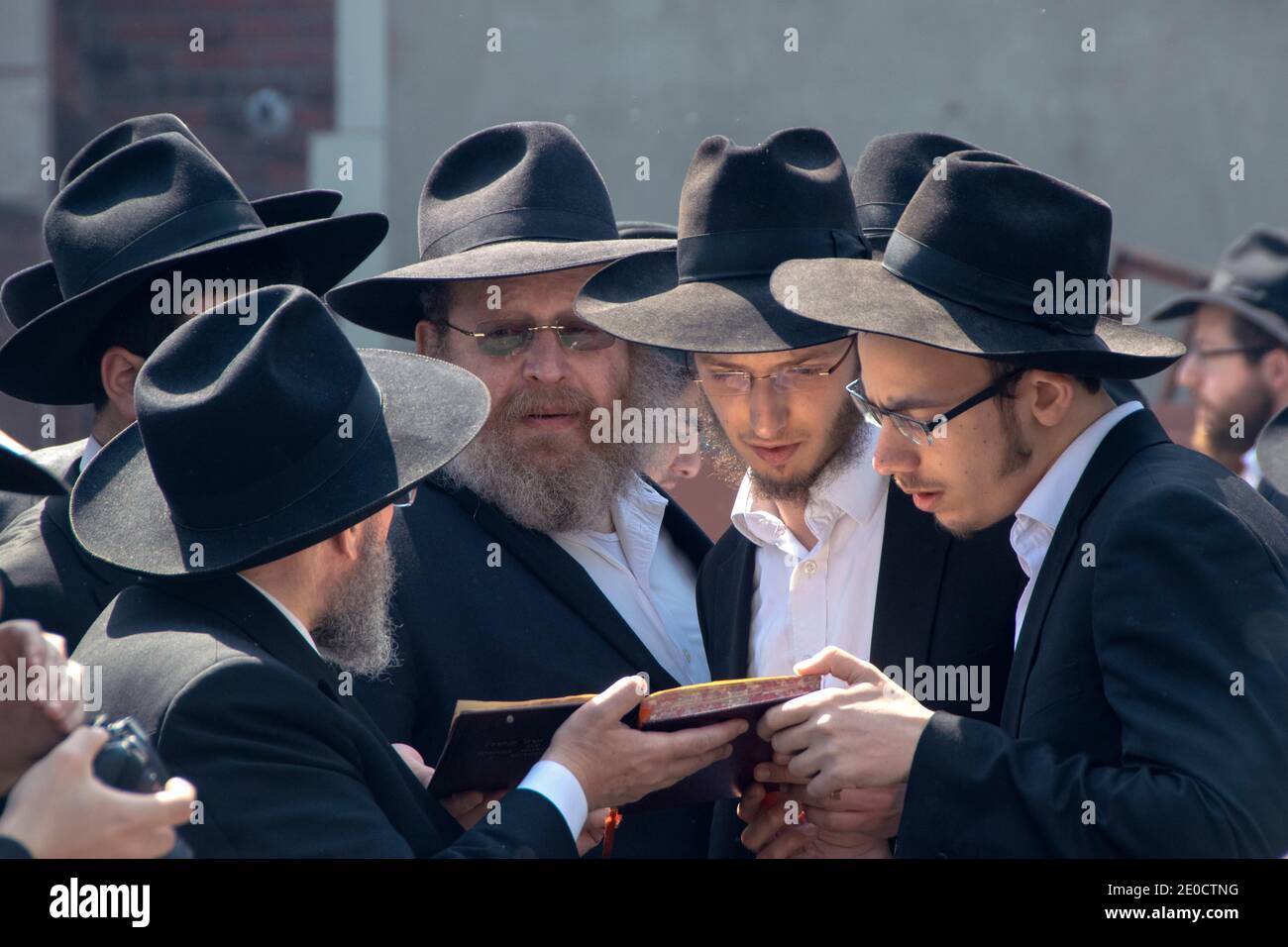 A group of Jewish men of varying ages share a prayer book at the annual ...