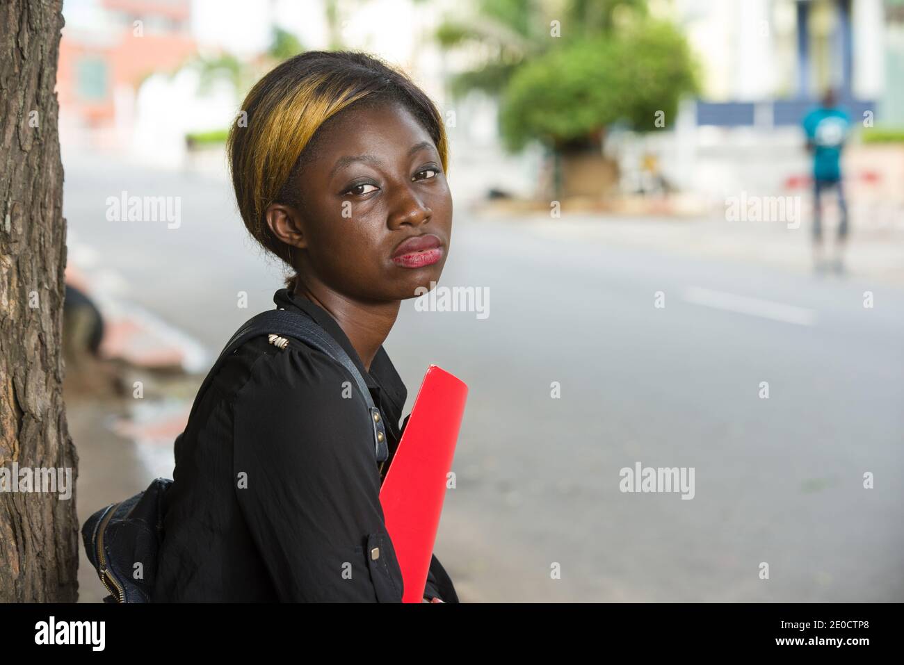 portrait of a shy student sitting on a tree in casual clothes holding ...