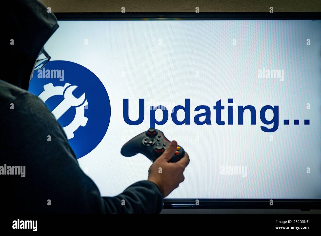 Hooded man holding a gaming controller in front of a screen showing an ...