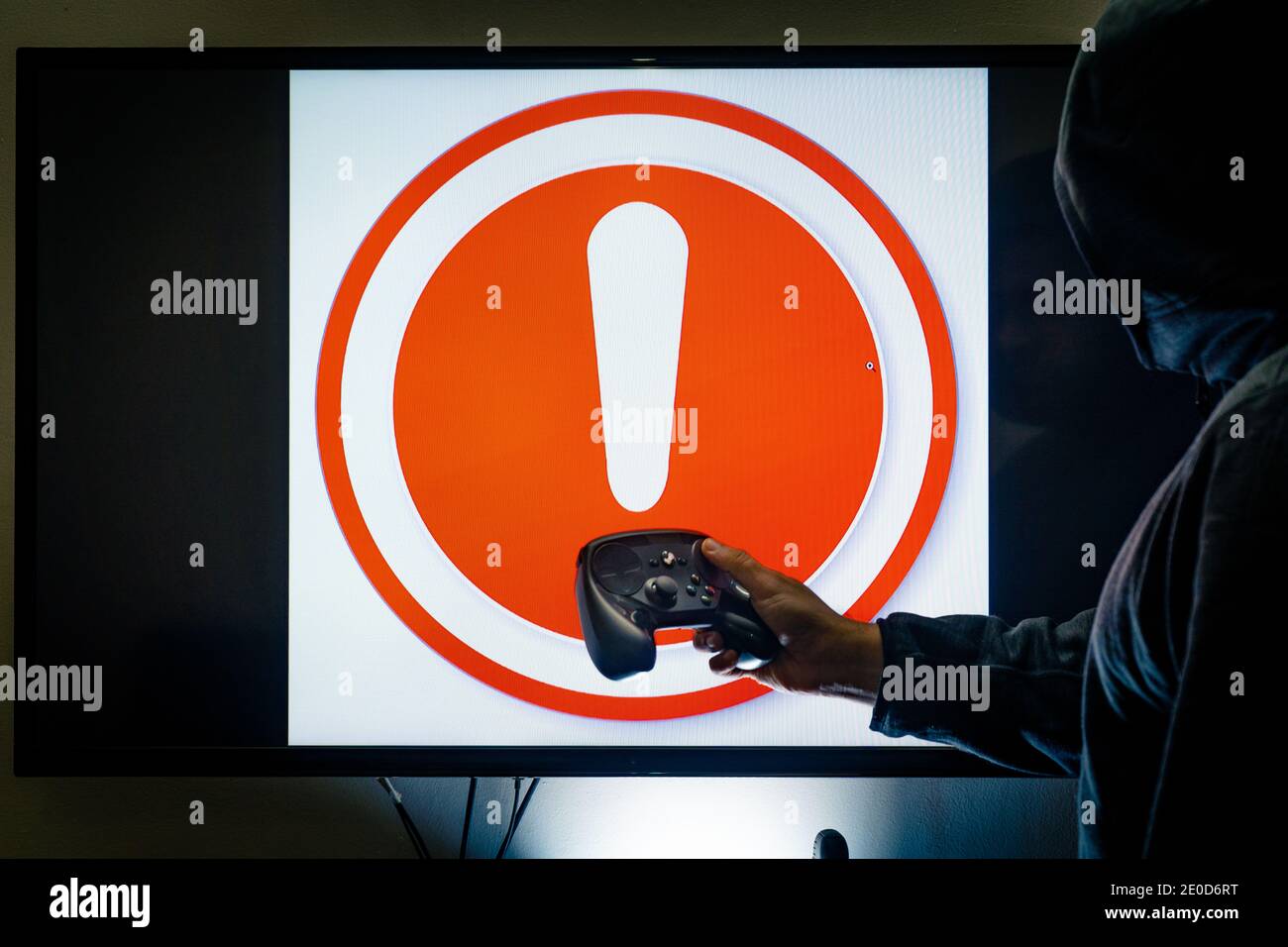 Man in hood holding controller in front of screen showing an alert red ...