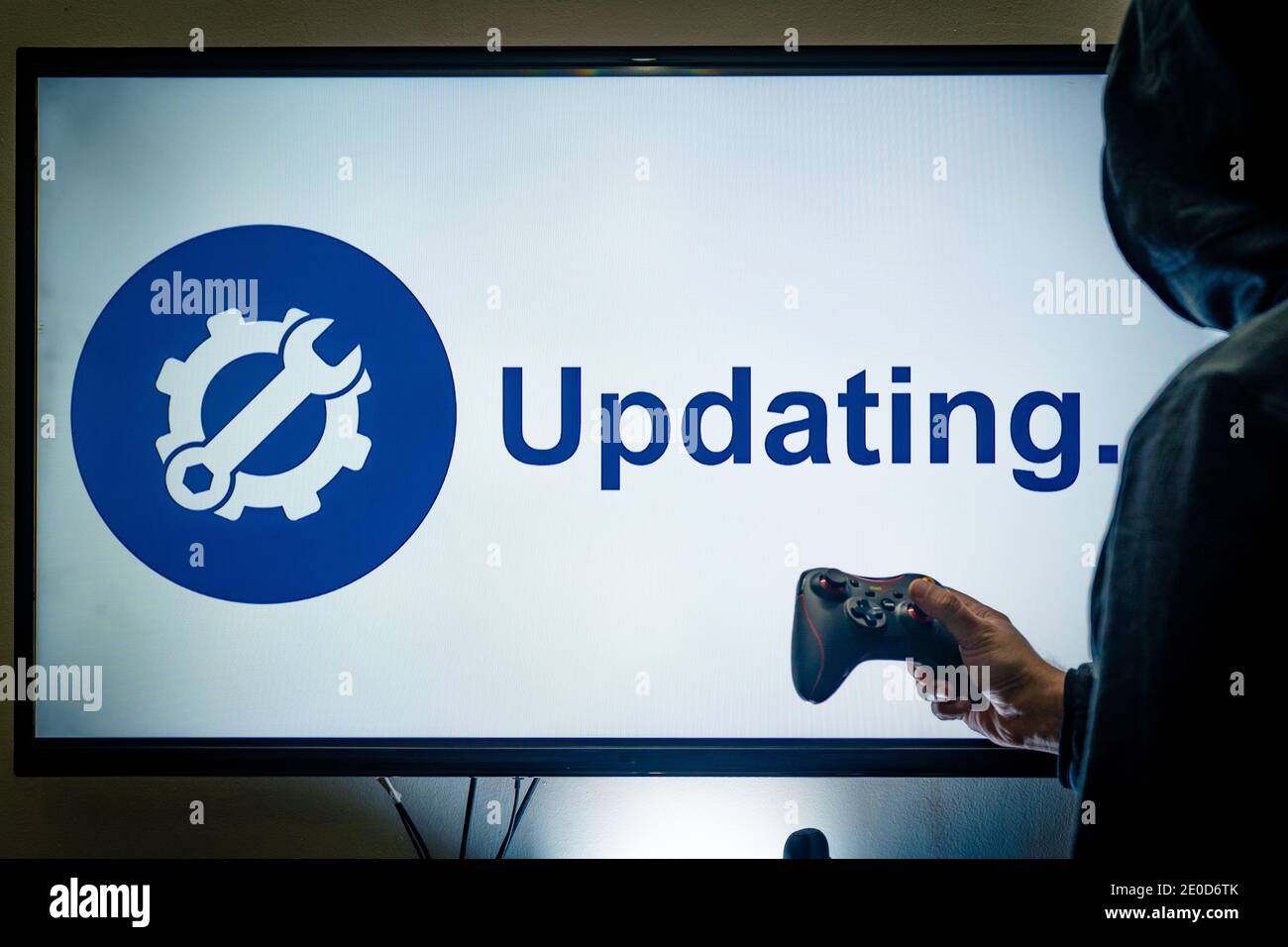 Hooded man holding a gaming controller in front of a screen showing an ...